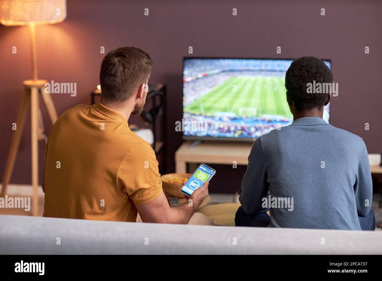 Back view of two men watching football match on TV and holding ...