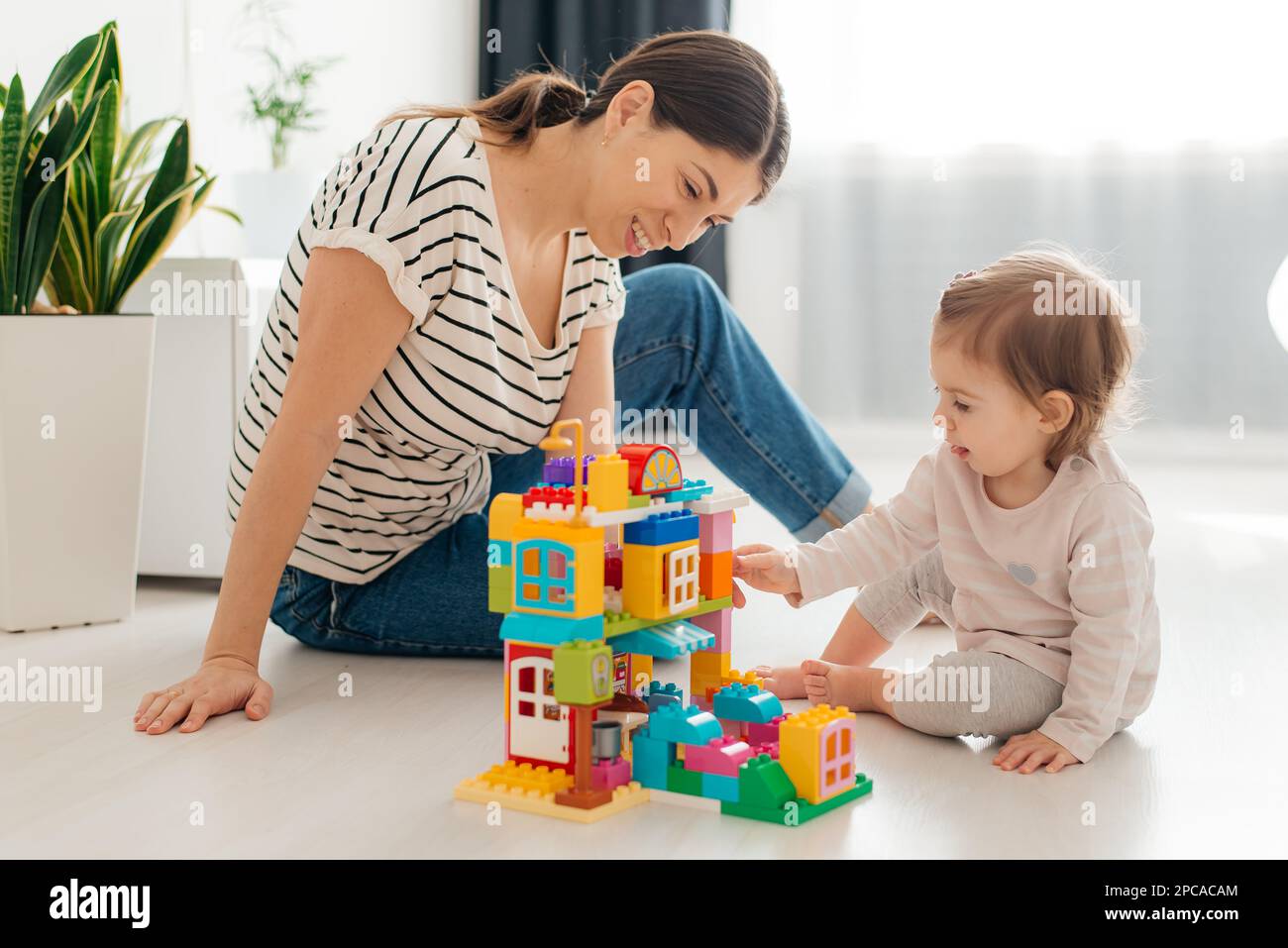 Laughing mother and little daughter playing colorful blocks ...