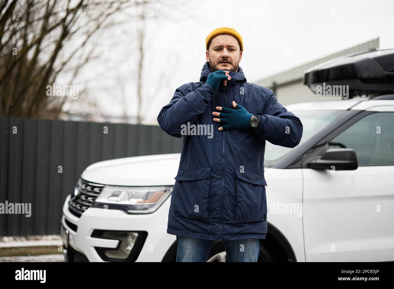 Man driver wear jacket and yellow hat against his american SUV car with ...