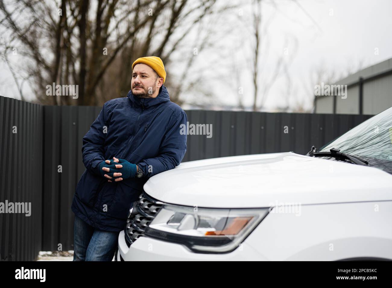 Man driver wear jacket and yellow hat against leaned on the hood of ...