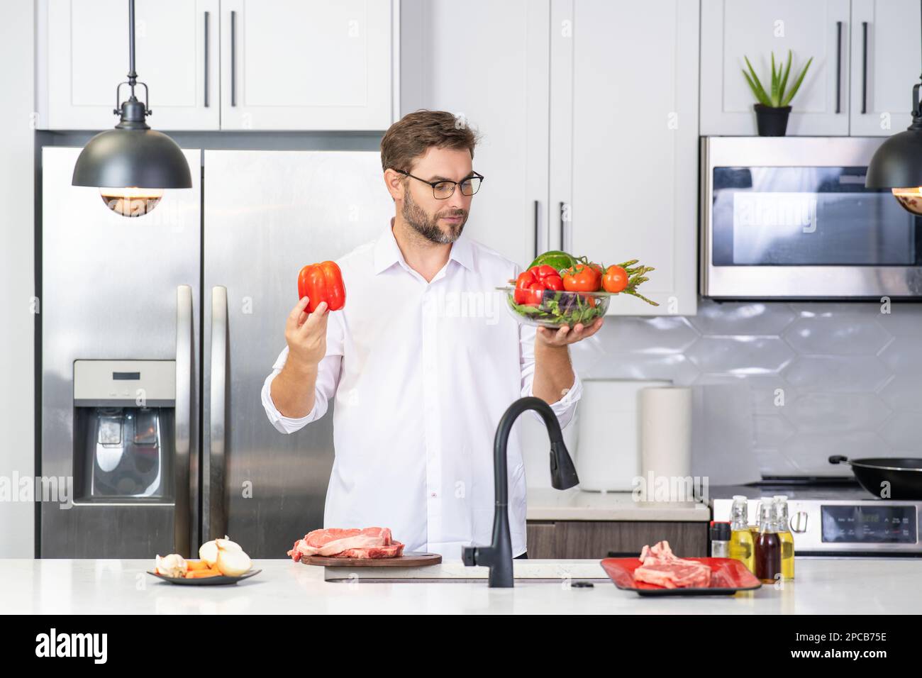 Handsome man cooking salad in kitchen. Guy leaning on kitchen with ...
