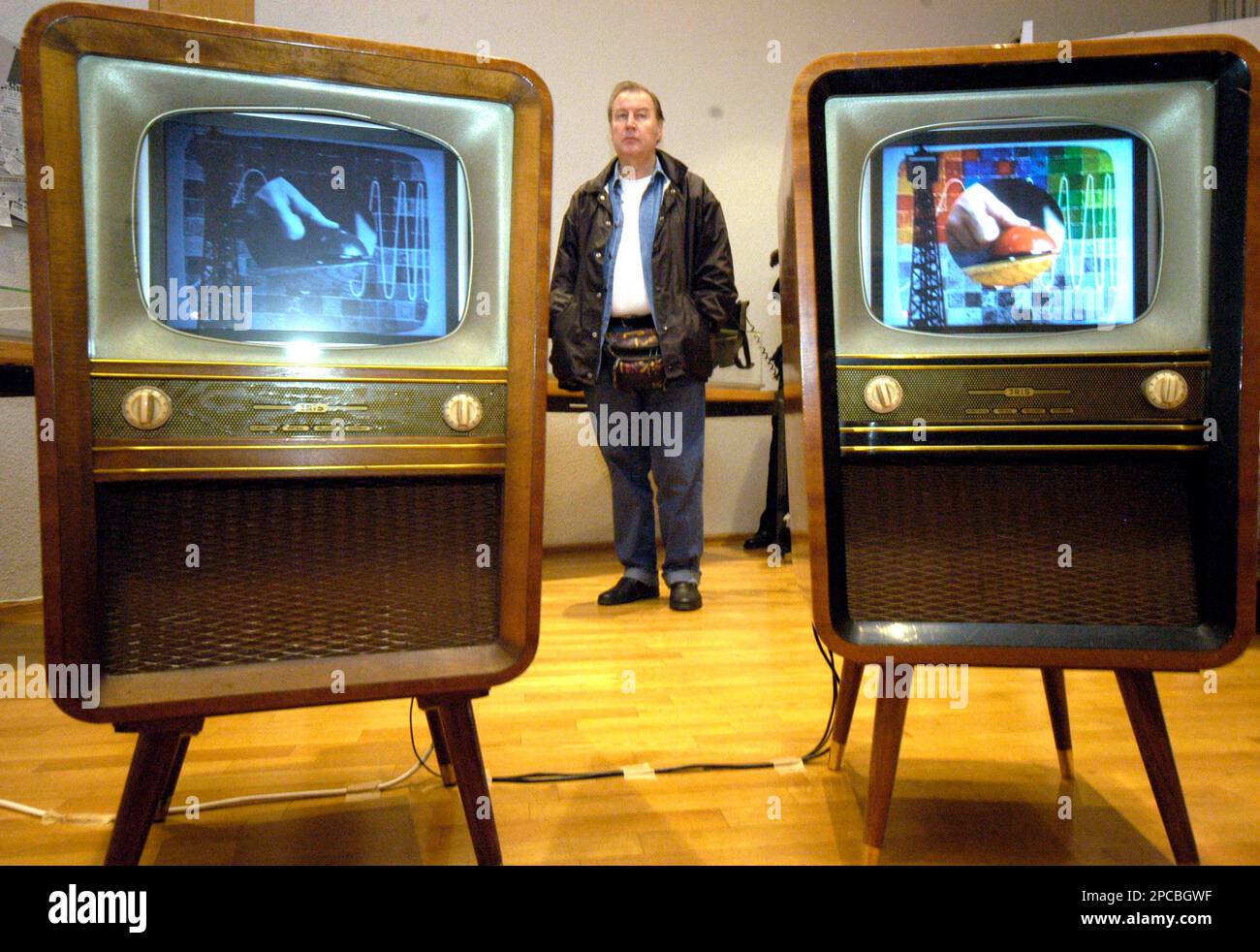 A man stands behind a black/white, left, and color, right, TV screens ...