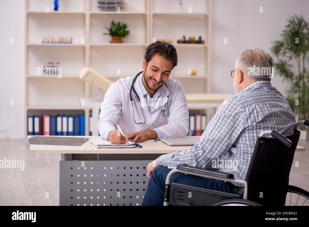 Old male patient in wheelchair visiting young male doctor Stock Photo ...