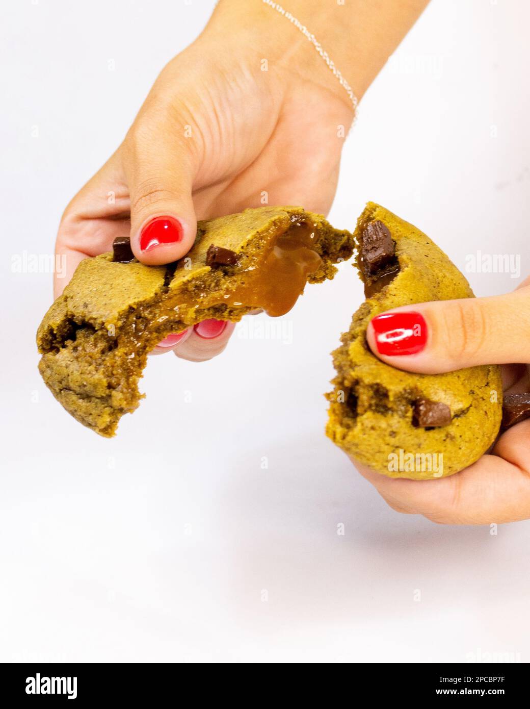A vertical shot of hands tearing a chocolate chip cookie with a caramel ...