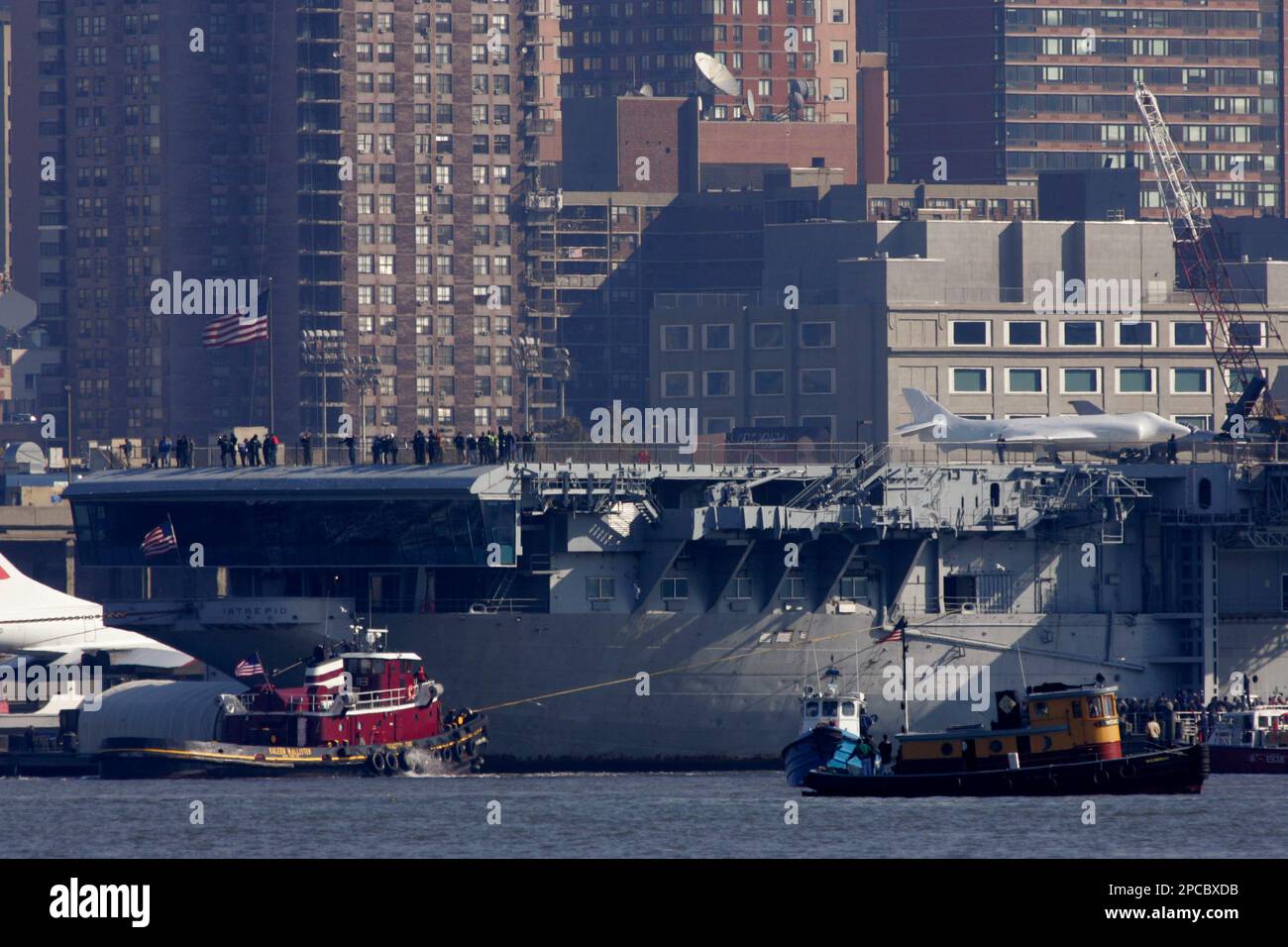 A tugboat pulls on a taut line connected to the USS Intrepid in its ...