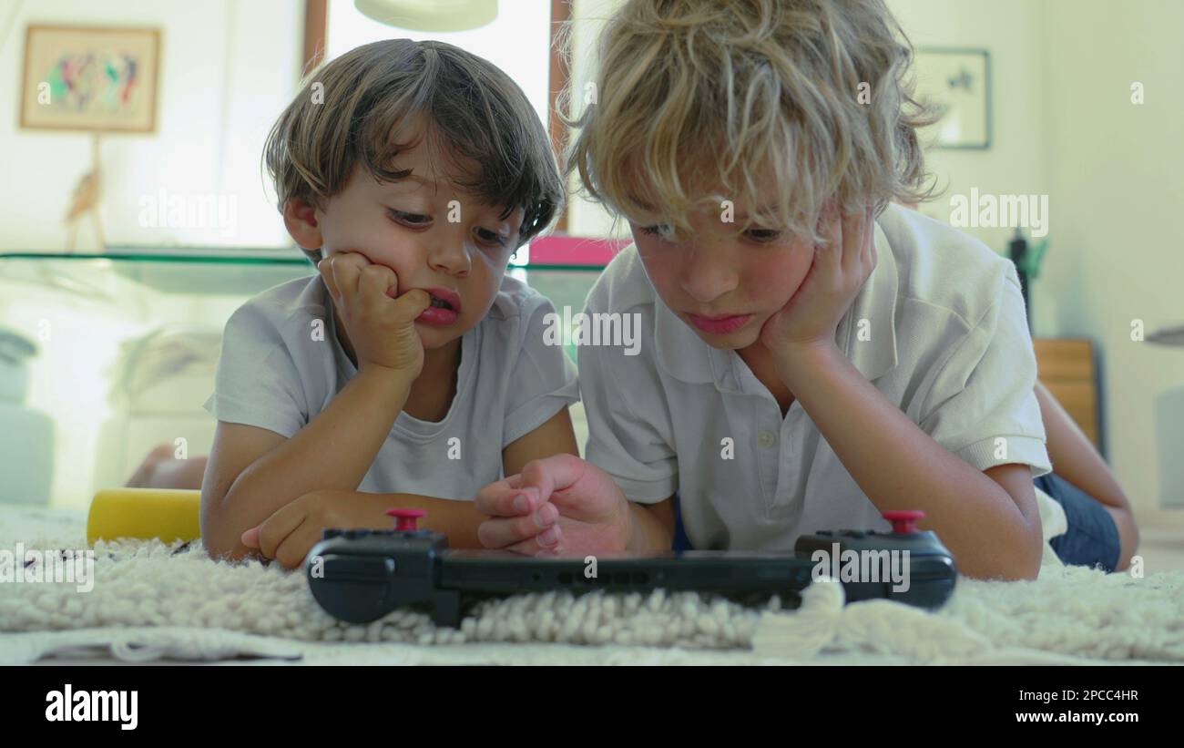 Two little boy staring at tablet screen laid on floor at living room ...