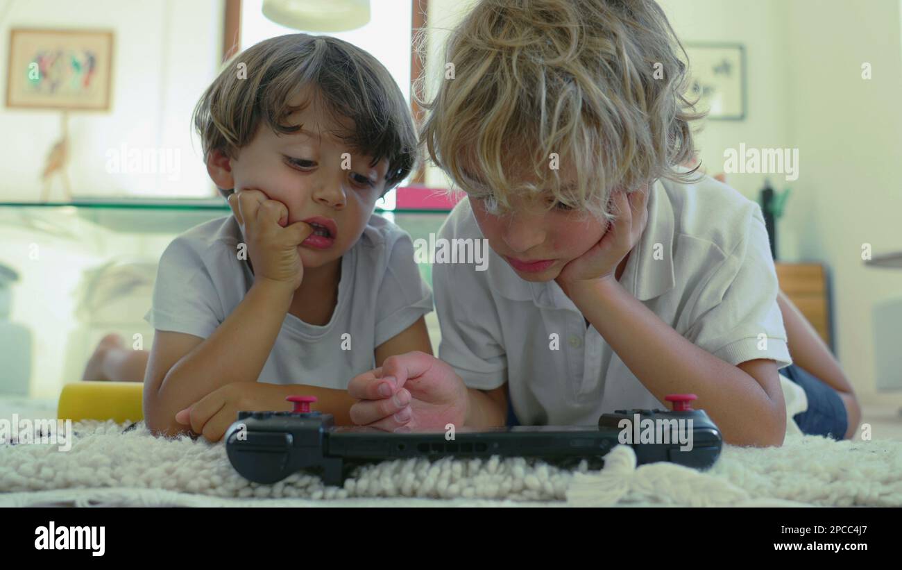 Two little boy staring at tablet screen laid on floor at living room ...