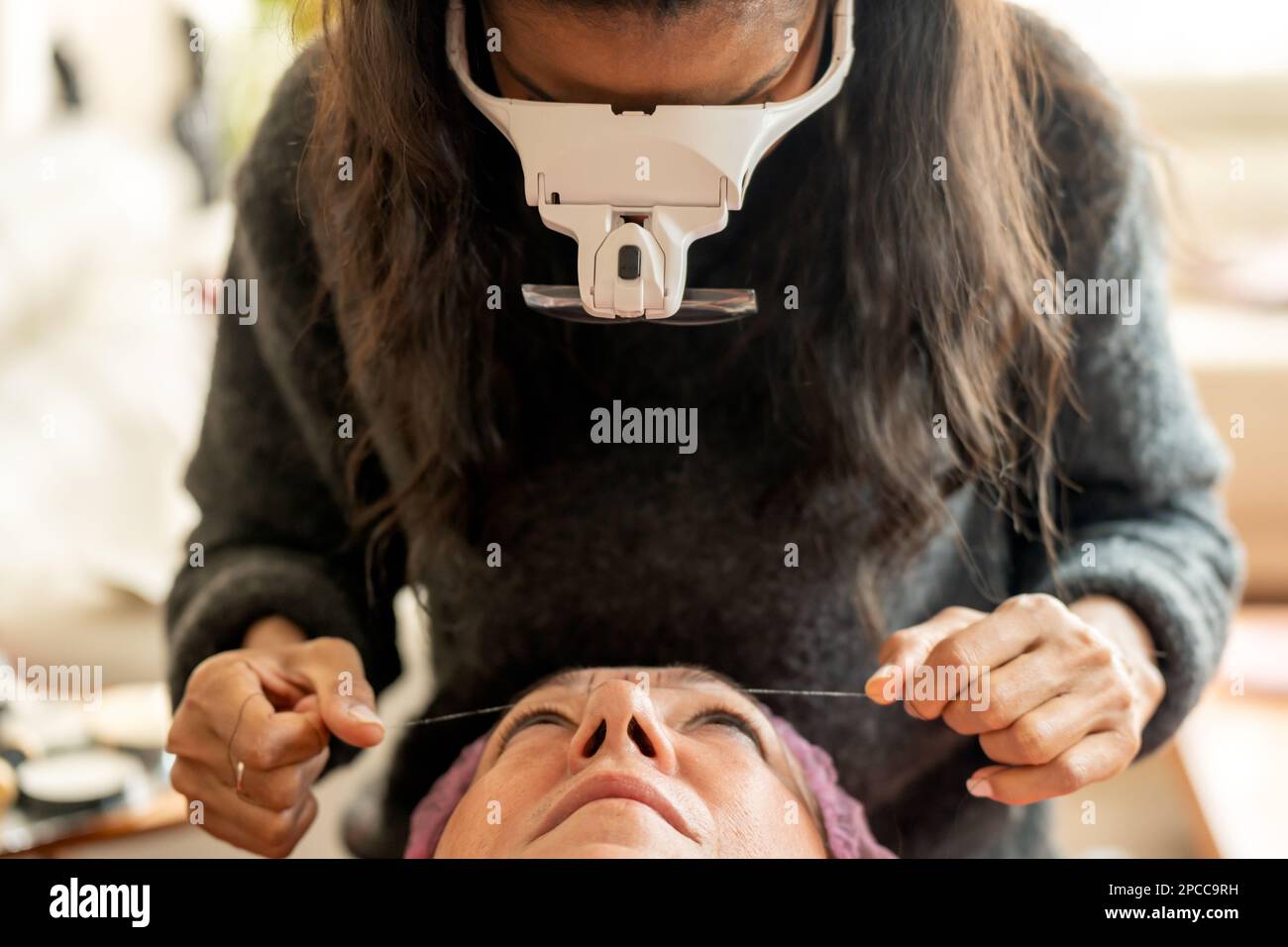 Crop cosmetologist wearing goggles with magnifying glass while ...
