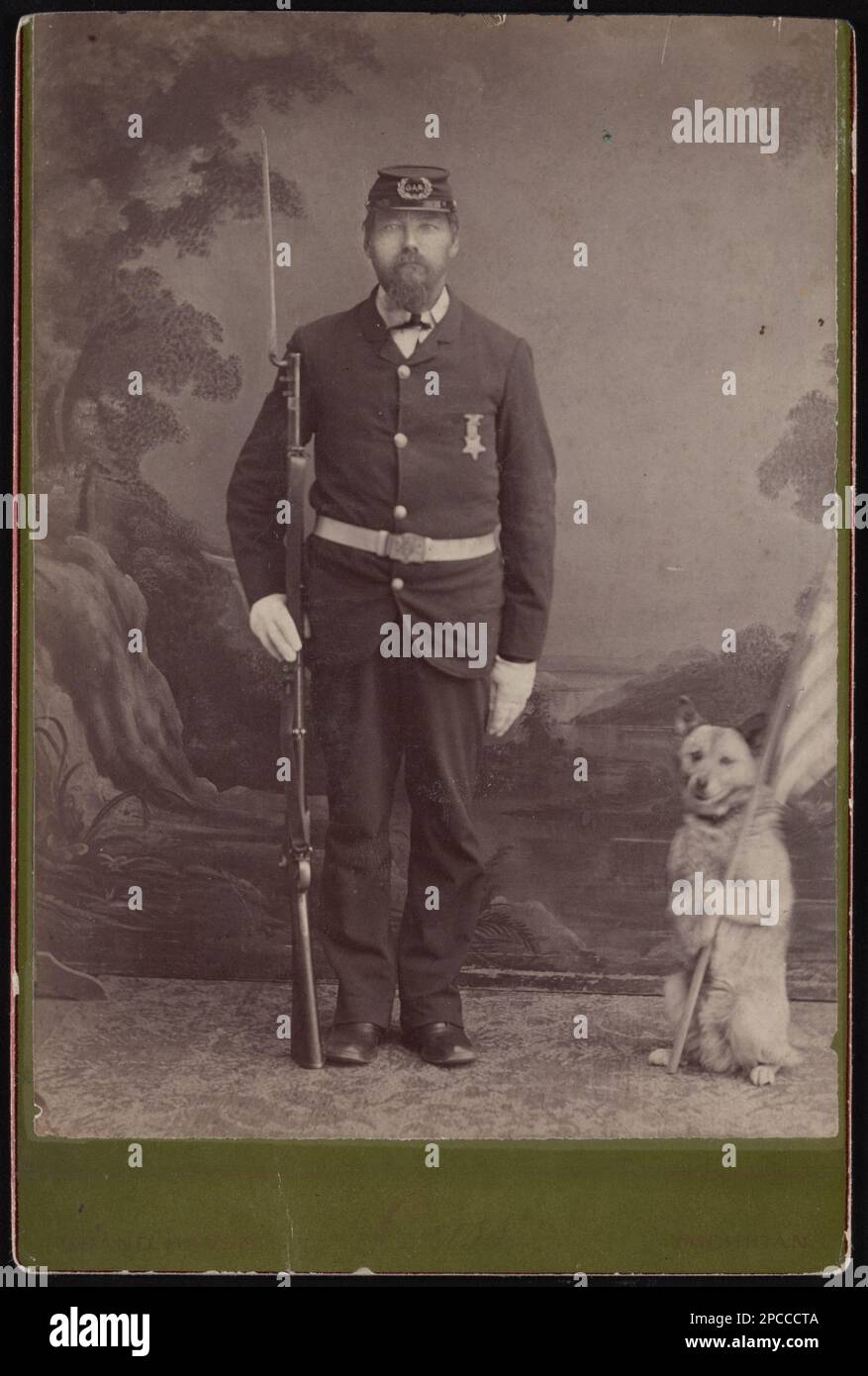 Civil War veteran holding bayoneted rifle and dog holding flag in front of painted backdrop ...