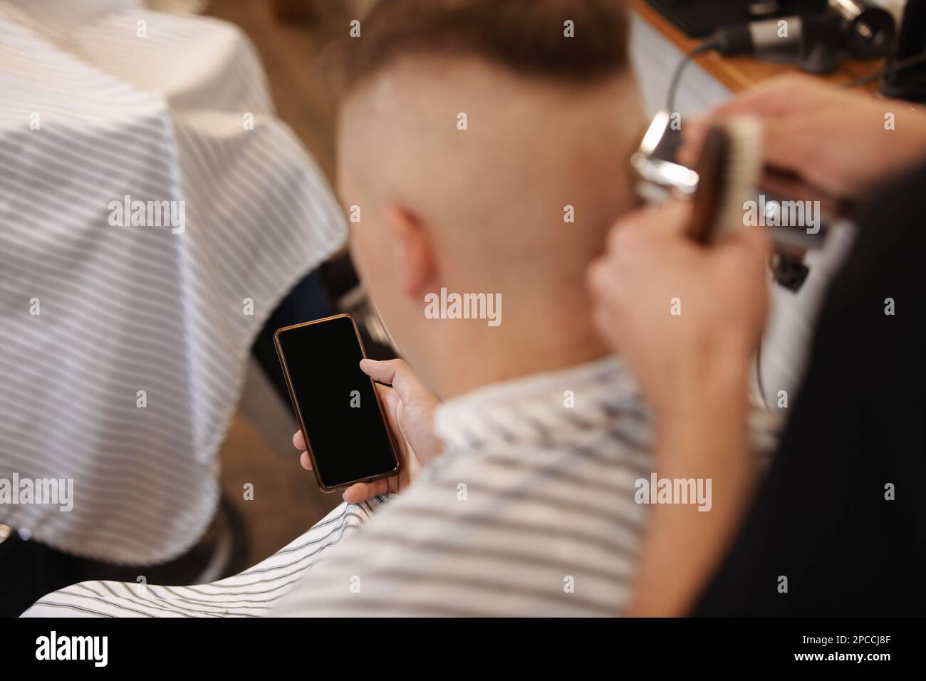 Back view of client uses smartphone during haircut. Barber with ...