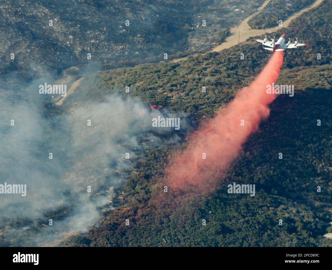 An aerial tanker makes a retardant drop as flames creep up a ridge line ...