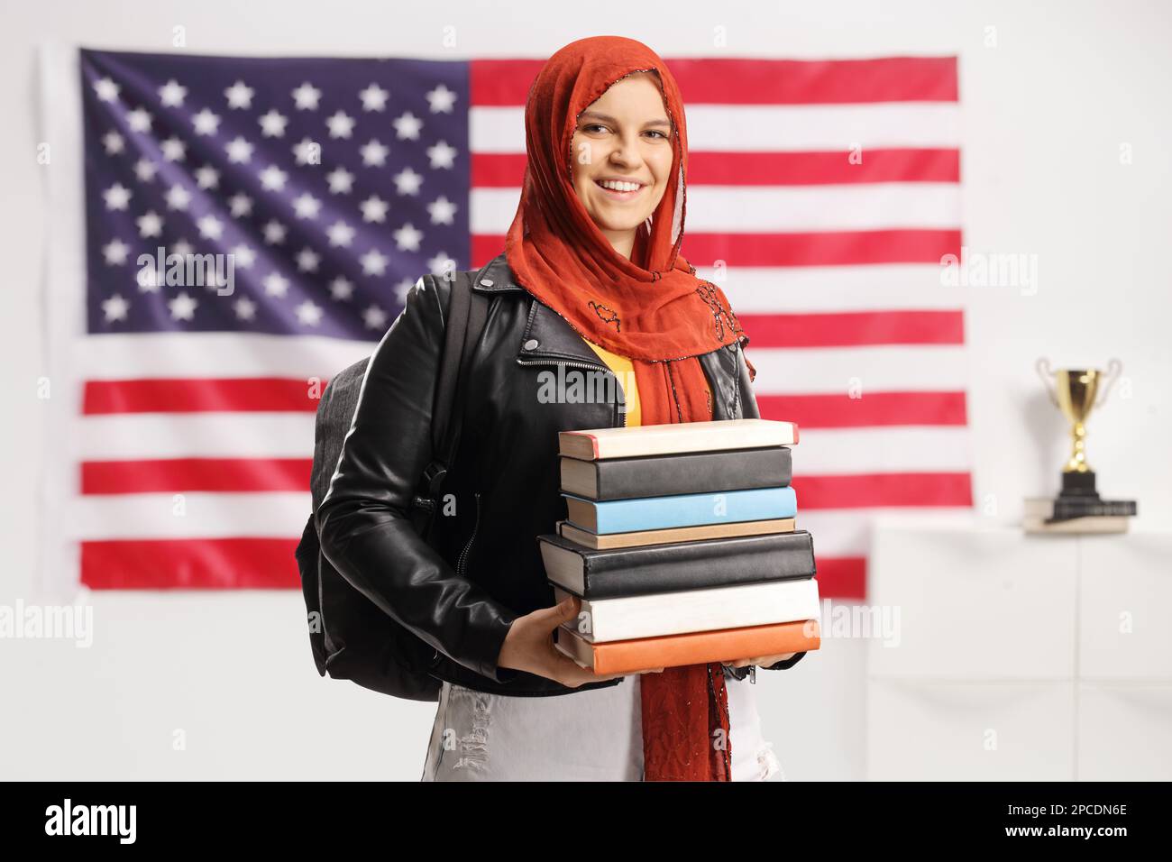 Muslim female student with a hijab carrying a pile of books and smiling ...