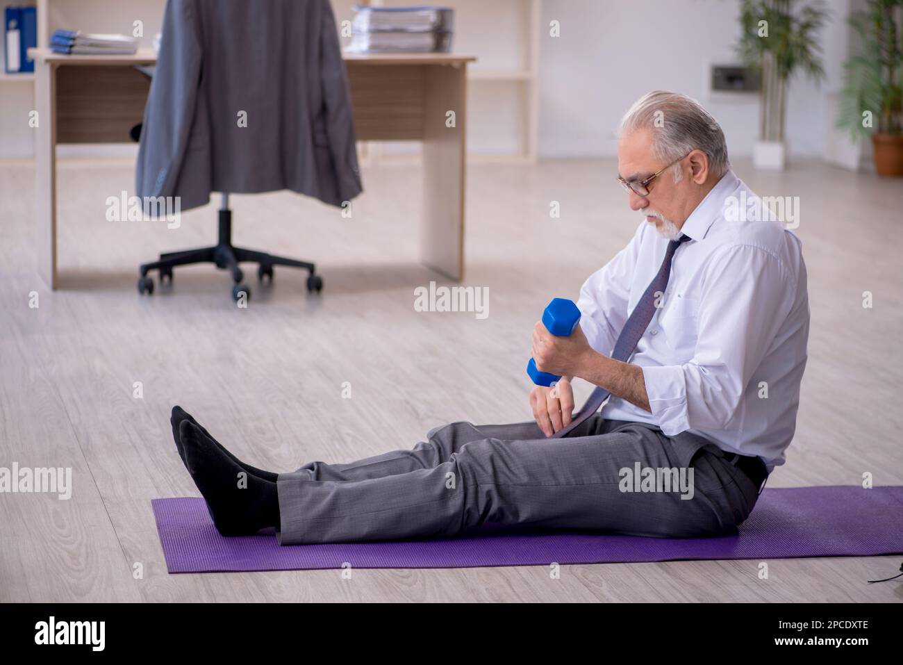Old employee doing sport exercises during break Stock Photo - Alamy