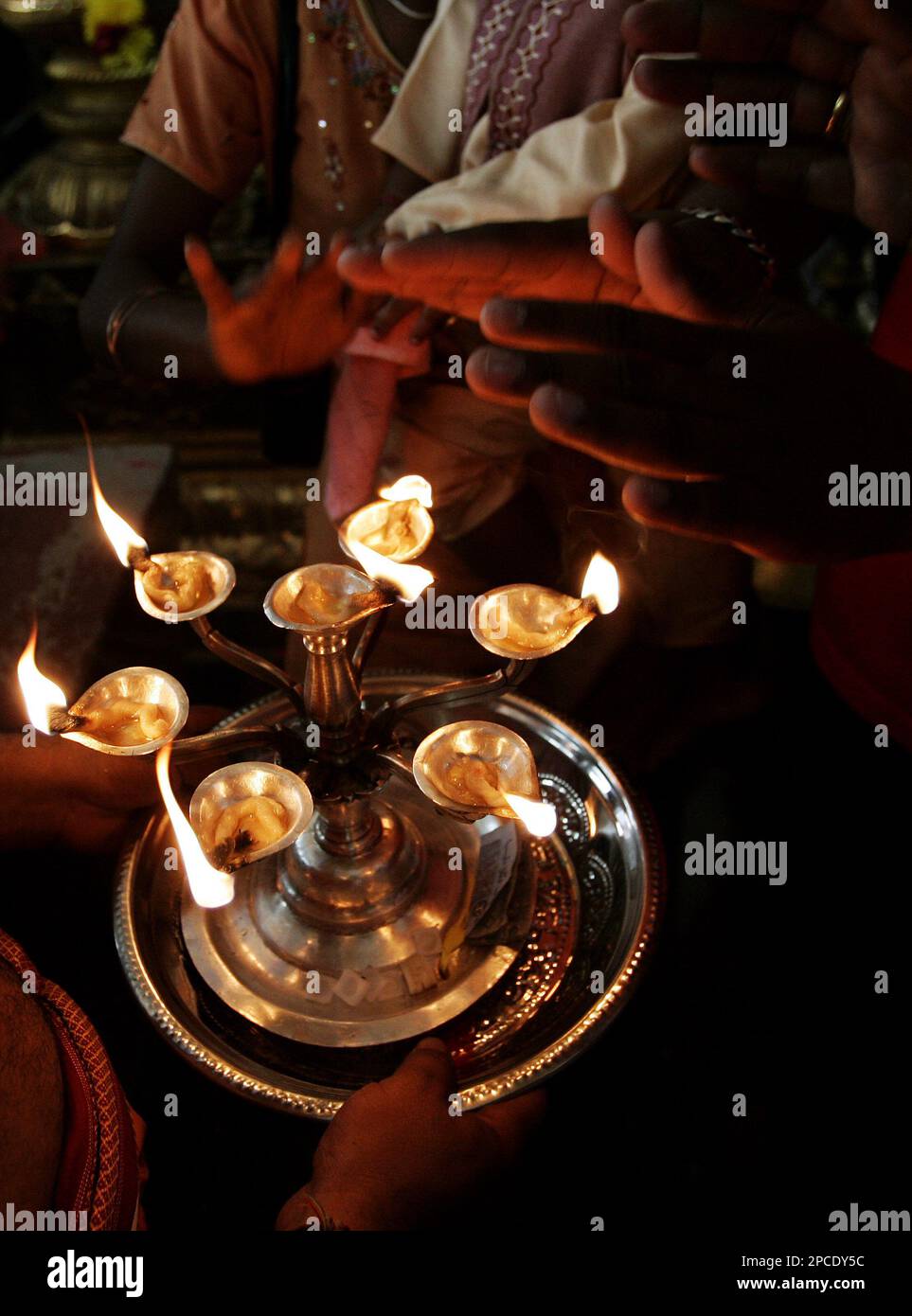 Hindu devotees make their offerings through a lamp carried by a priest ...