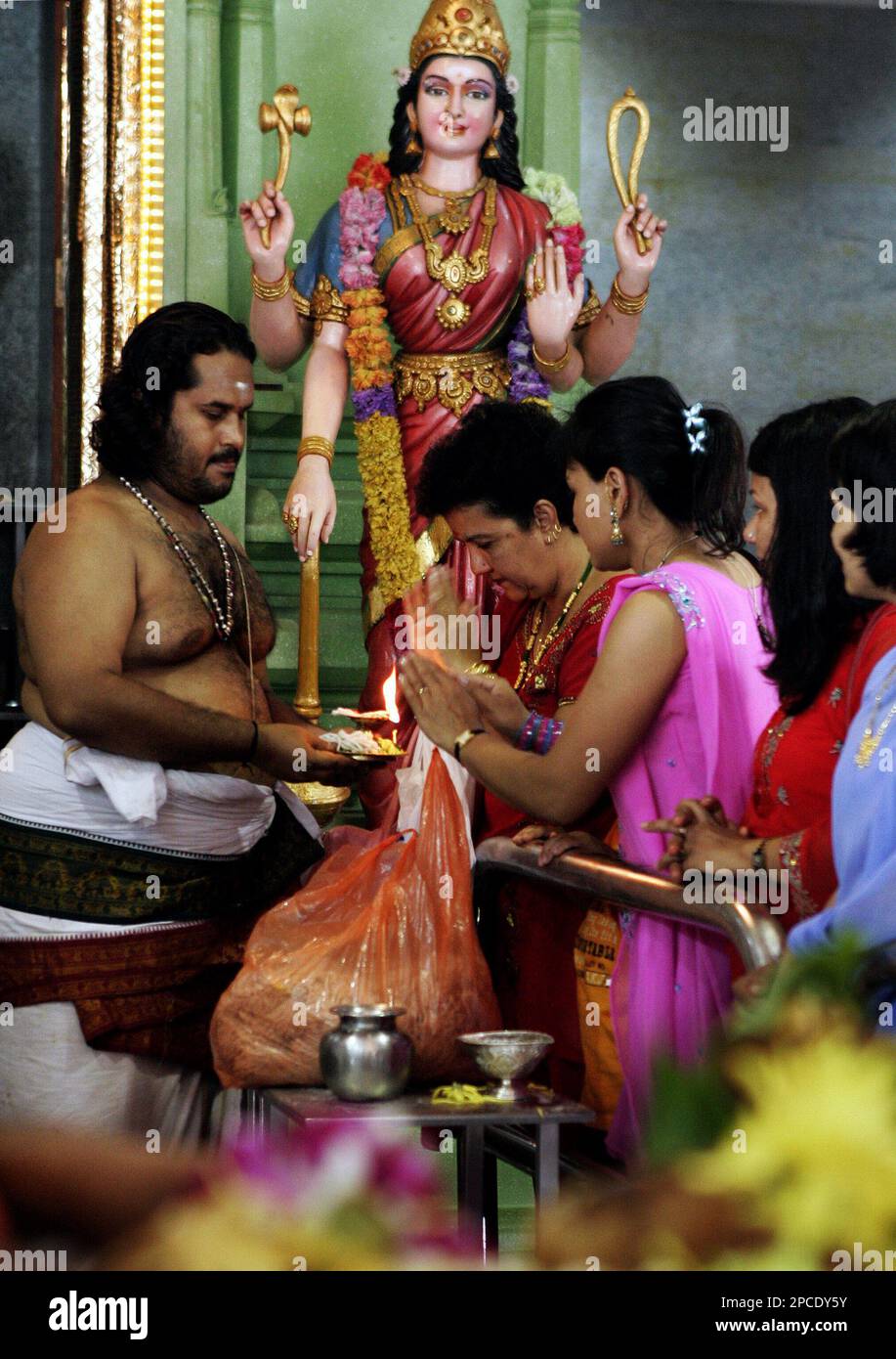 Hindu devotees make their offerings through a lamp carried by a priest ...