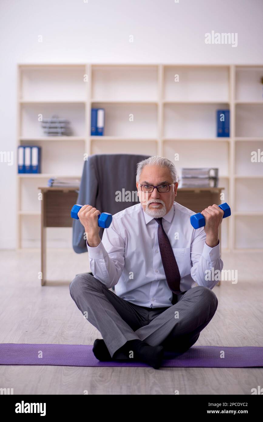 Old employee doing sport exercises during break Stock Photo - Alamy