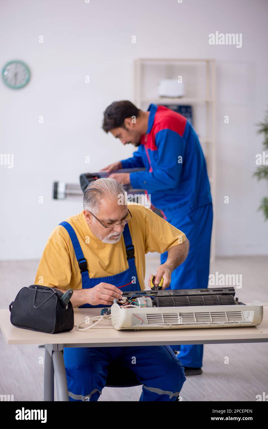 Two repairmen repairing air-conditioner at workshop Stock Photo - Alamy