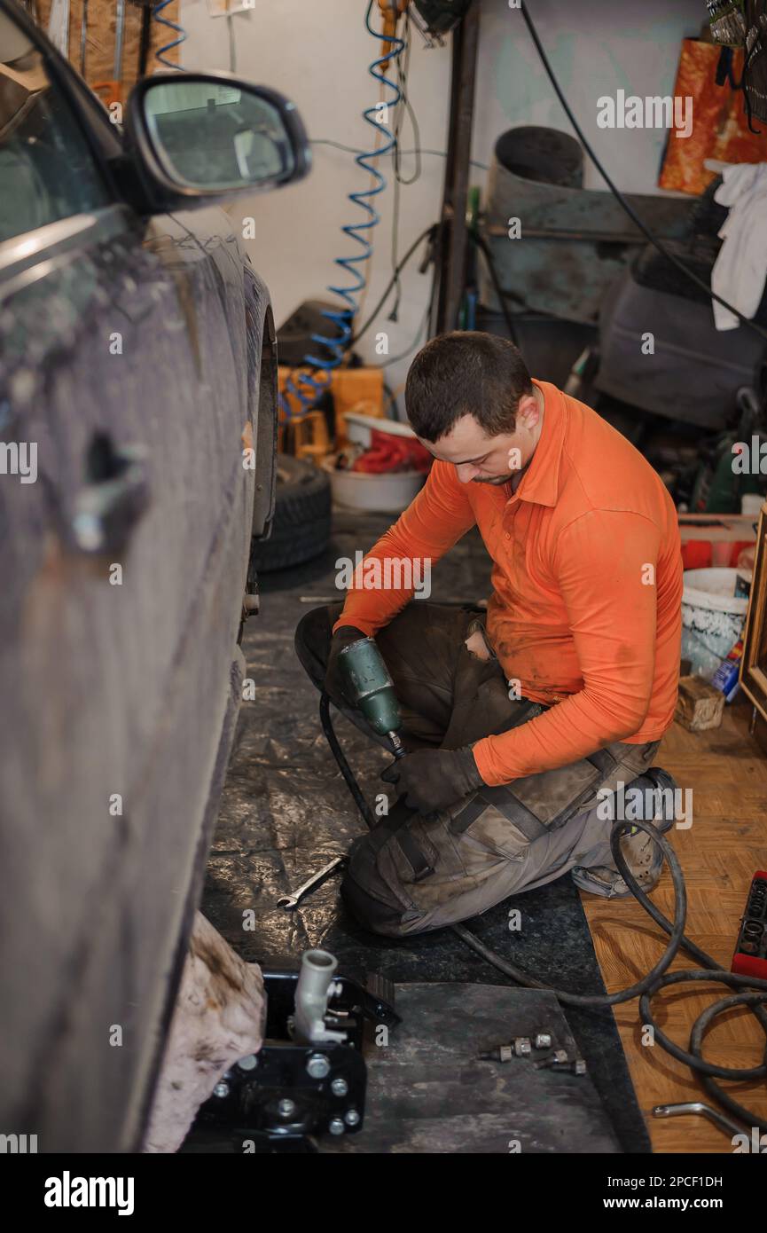 Mechanic repairs the undercarriage of the car. A man repairs a car in a ...