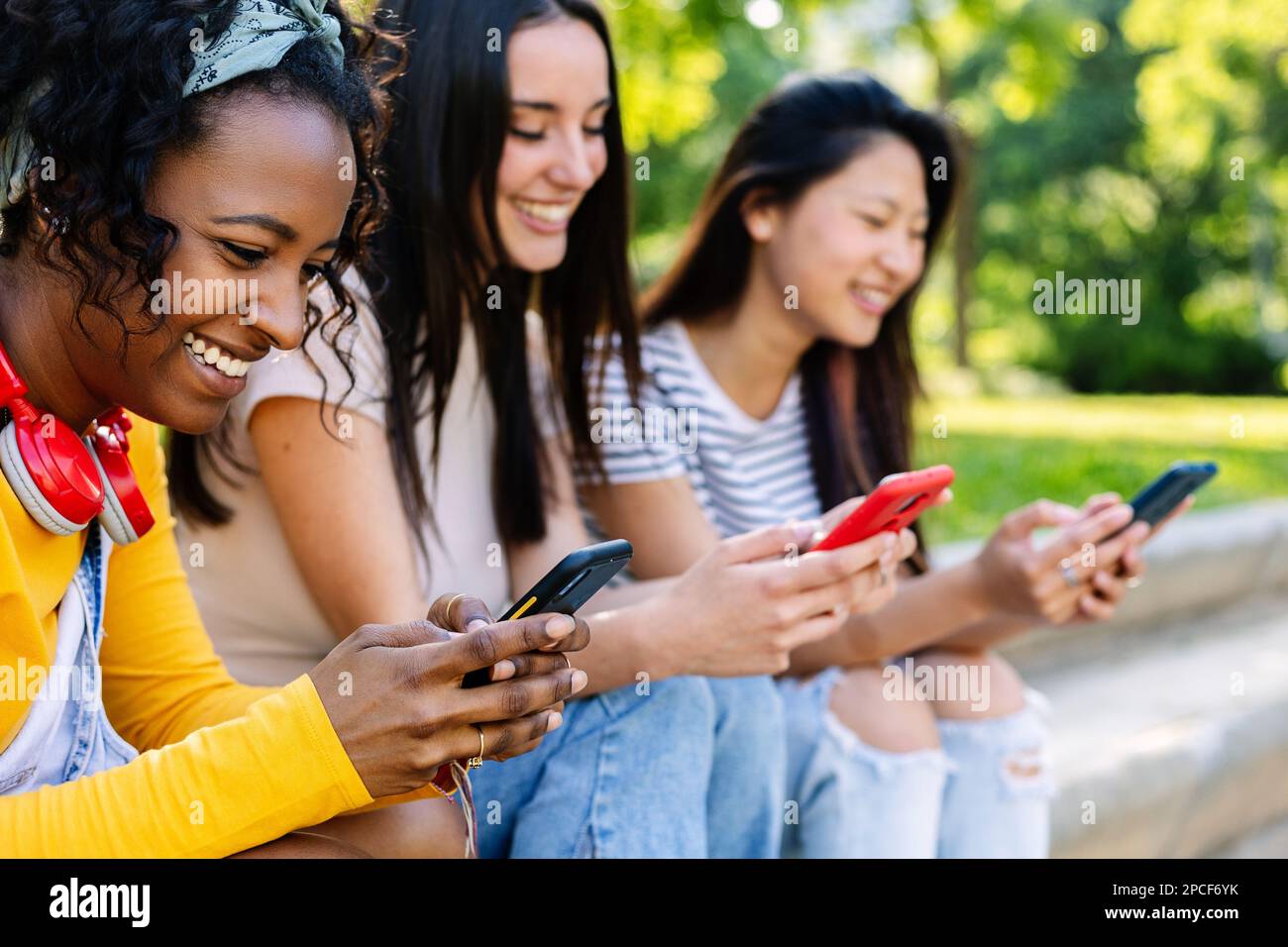 Three multiracial young women having fun using mobile phone outside ...