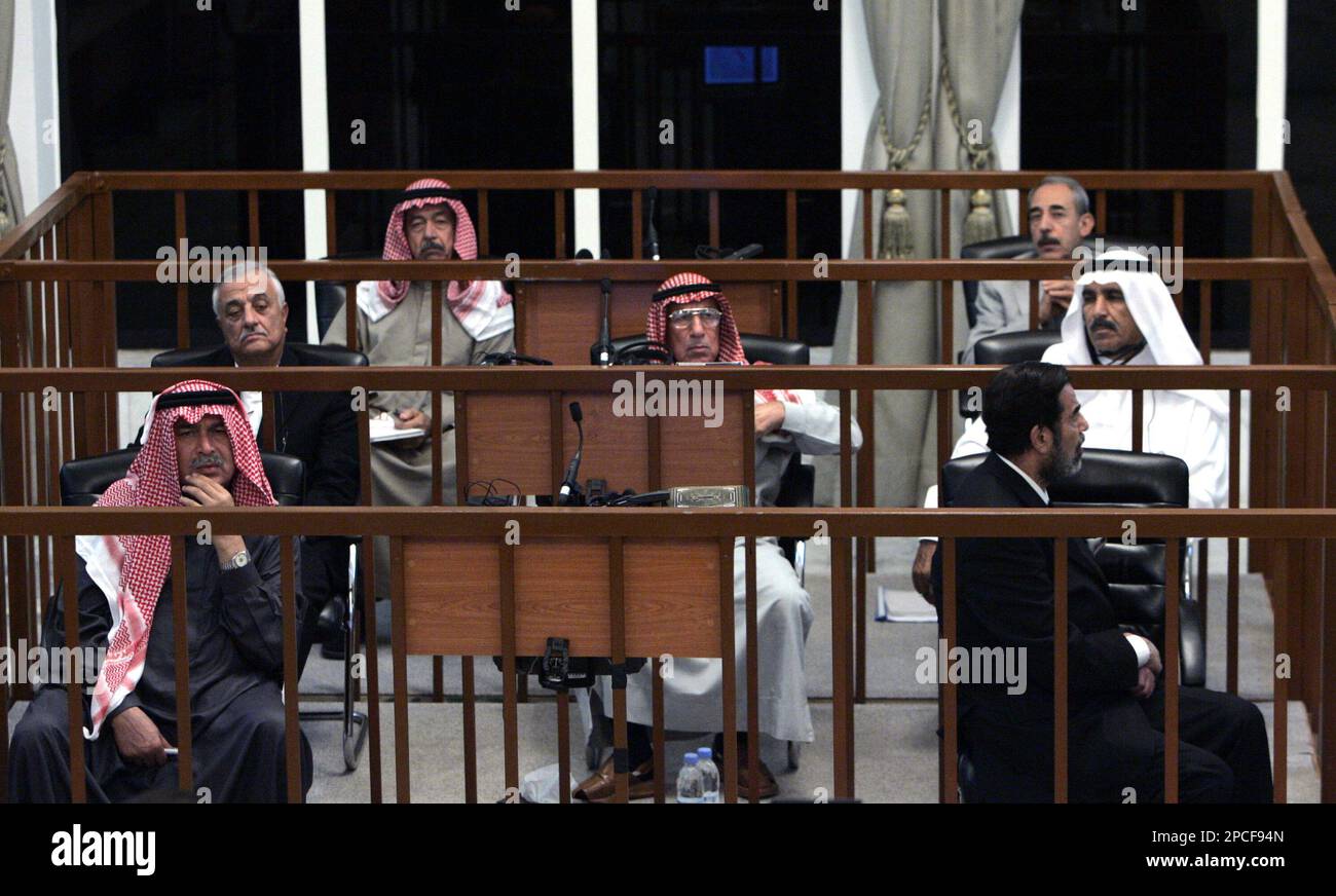 Former Iraqi dictator Saddam Hussein, right, turns and sits with his ...