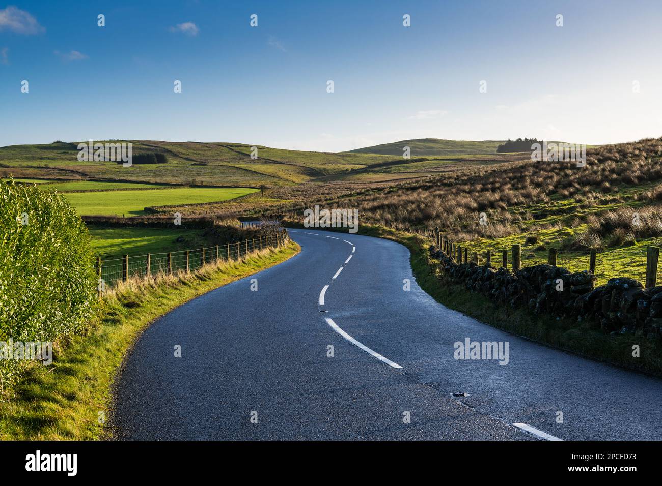 A scenic paved road winding through the lush green hills and fields of ...