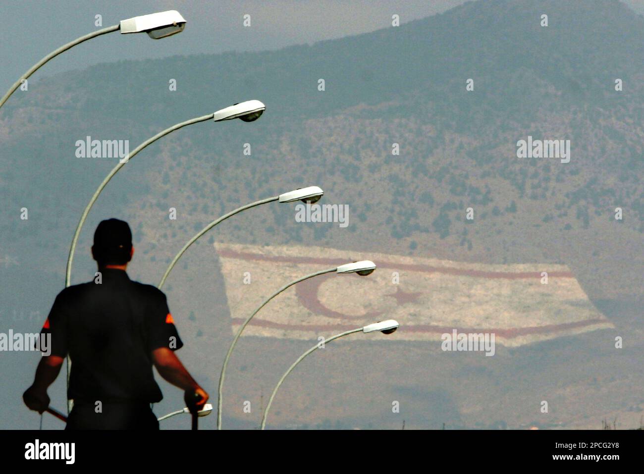 A Greek Cypriot fire fighter stands on a fire truck in front of a ...