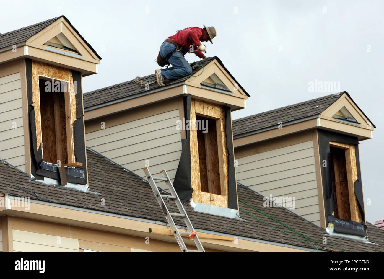 An unidentified roofer works to attach the shingles on one of the ...