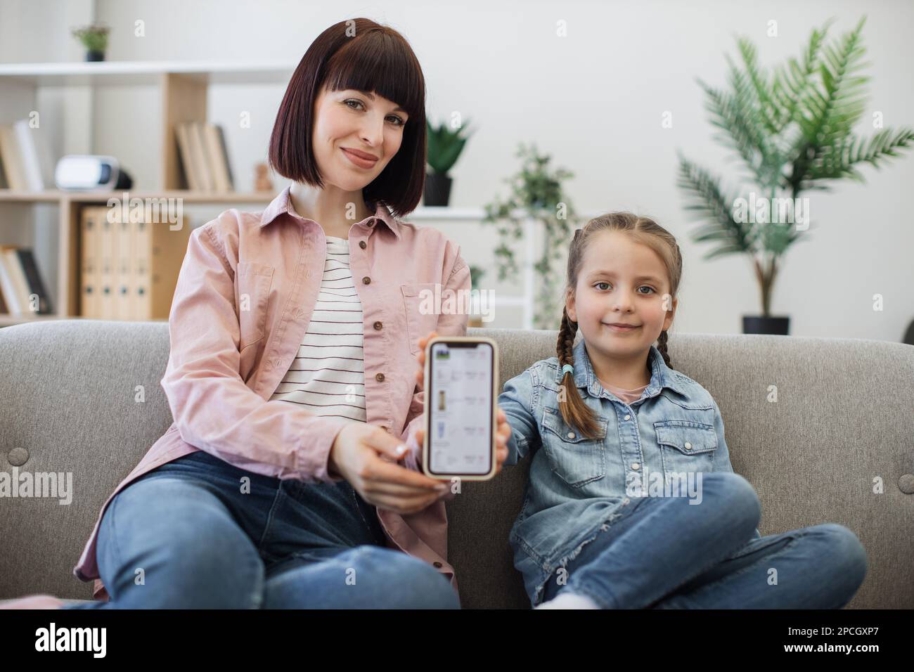 Charming young woman with little girl sitting on sofa at home and ...
