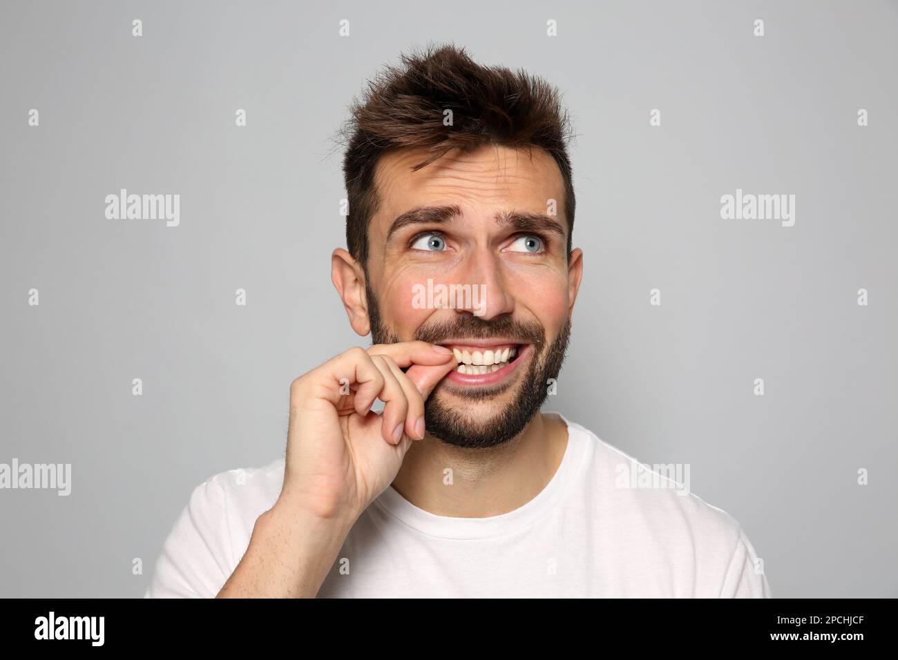 Man biting his nails on grey background Stock Photo - Alamy