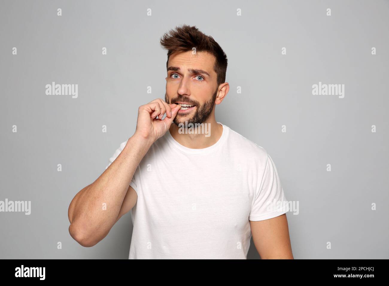 Man biting his nails on grey background Stock Photo - Alamy