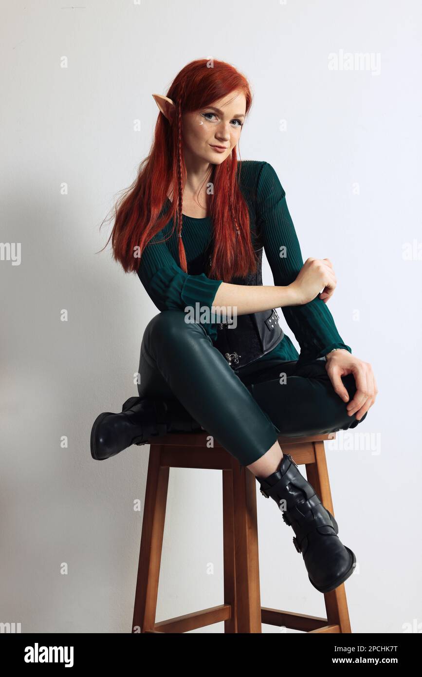 Beautiful redhead elf girl sitting on stool against light background ...
