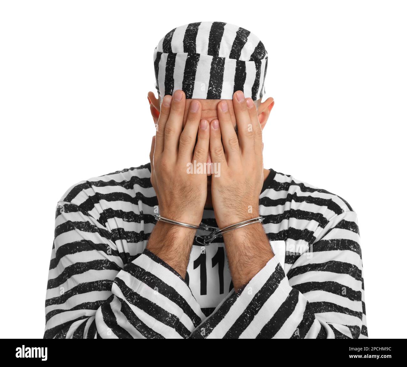 Remorseful prisoner in striped uniform with handcuffs hiding his face ...