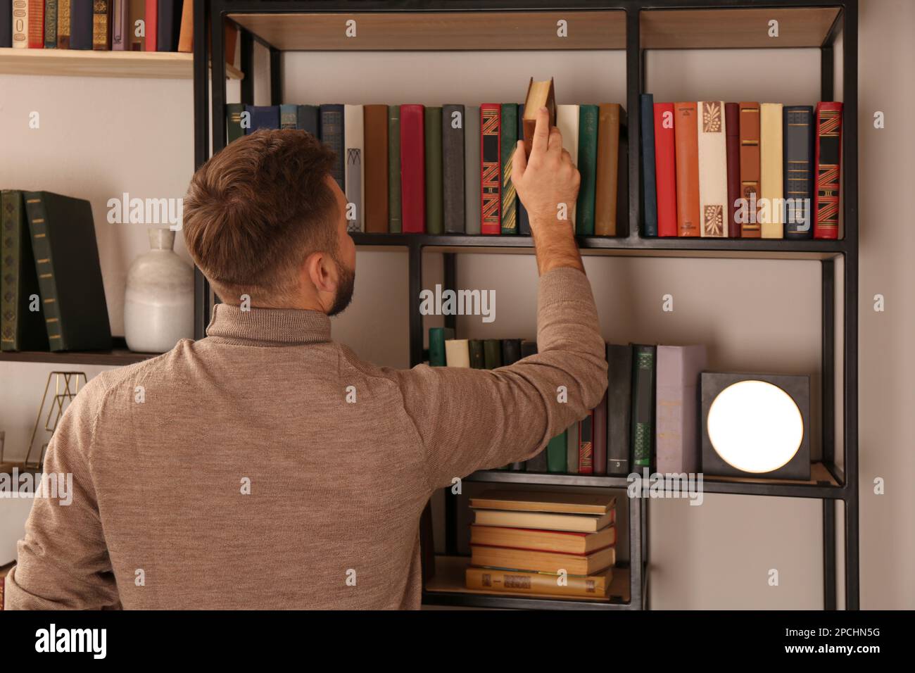 Young man choosing book on shelf in home library, back view Stock Photo ...