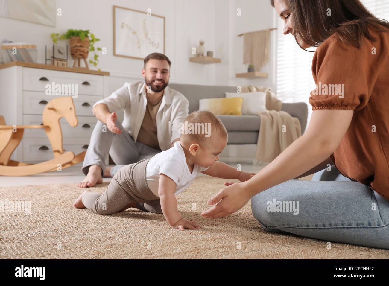 Happy parents helping their baby to crawl on floor at home Stock Photo ...