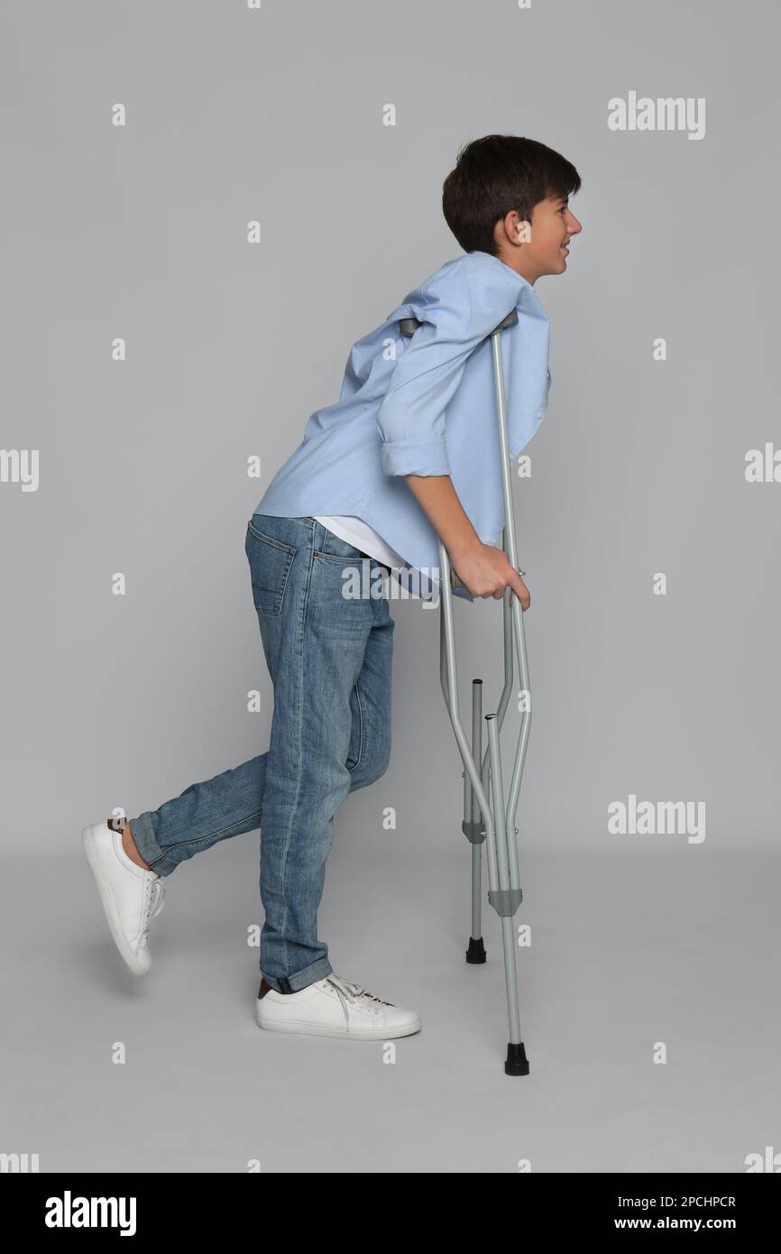 Teenage boy with injured leg using crutches on grey background Stock ...