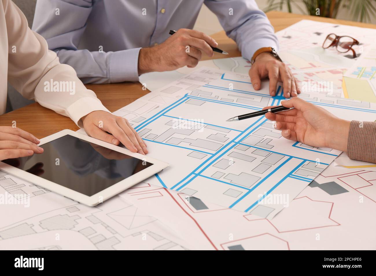Professional cartographers working with cadastral map at table, closeup ...