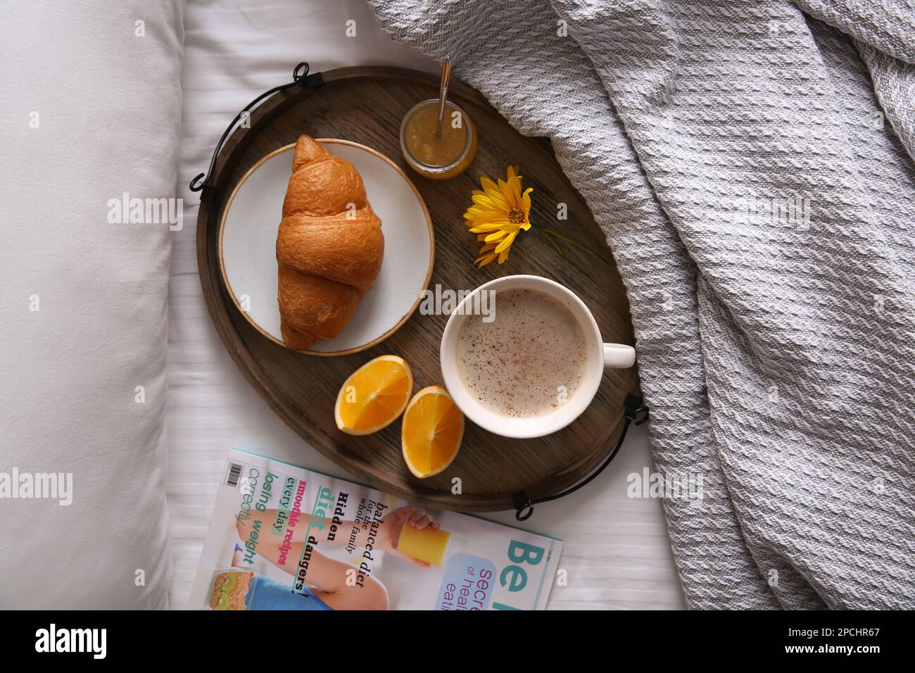 Wooden tray with delicious breakfast and beautiful flower on bed, flat ...