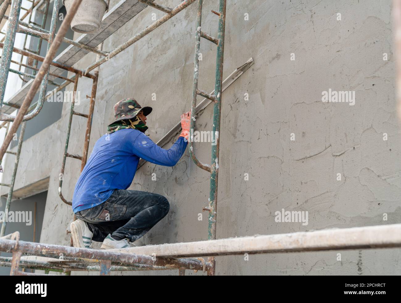 Construction worker with a long trowel to plaster the wall by hand in ...