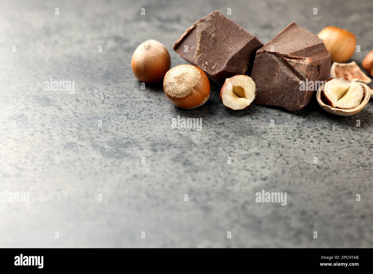 Delicious chocolate chunks and hazelnuts on grey table. Space for text ...