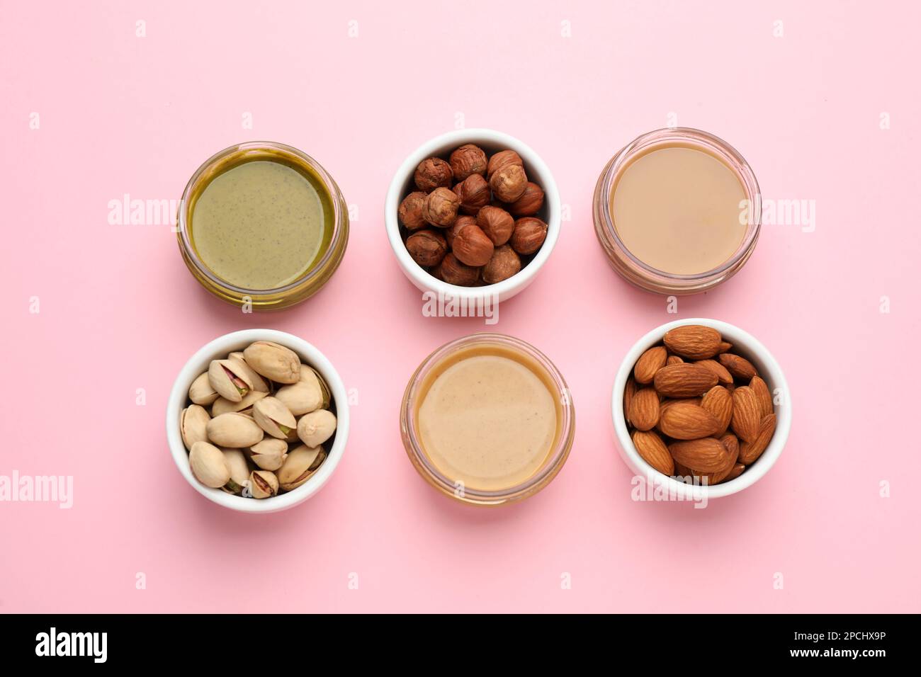 Different types of delicious nut butters and ingredients on pink ...