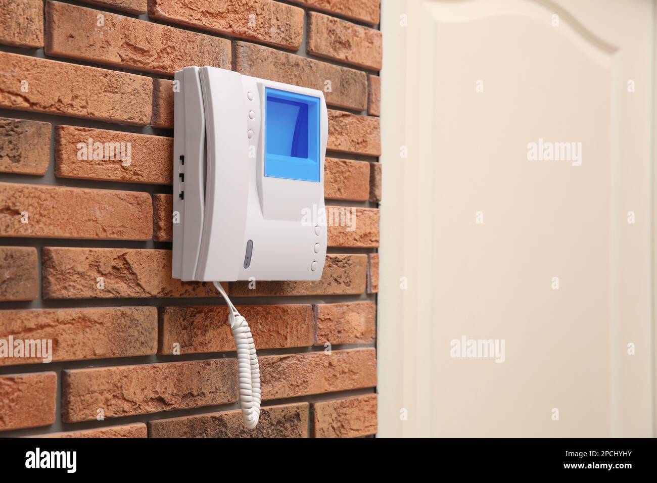 Modern intercom system with handset on red brick wall indoors, space ...