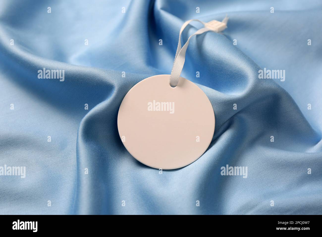 Blank white tag on light blue silky fabric, closeup. Space for text ...