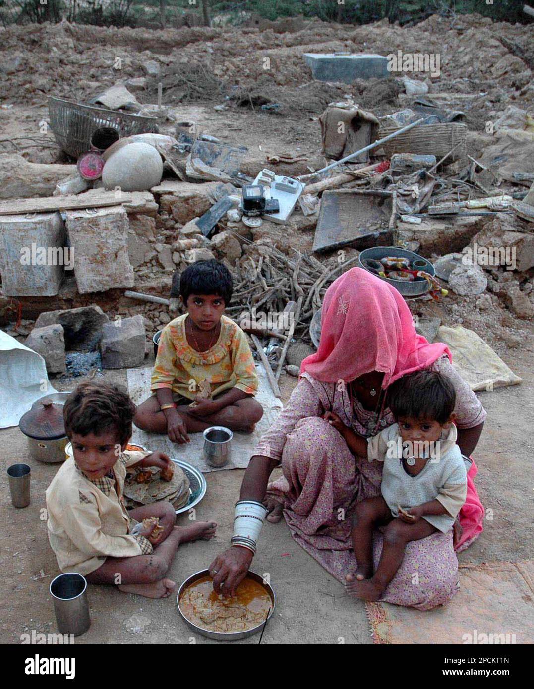 A woman and her children eat their meal in front of their collapsed ...
