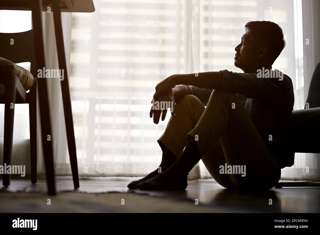 Depressed and frustrated Asian man sits on the living room floor, dark ...
