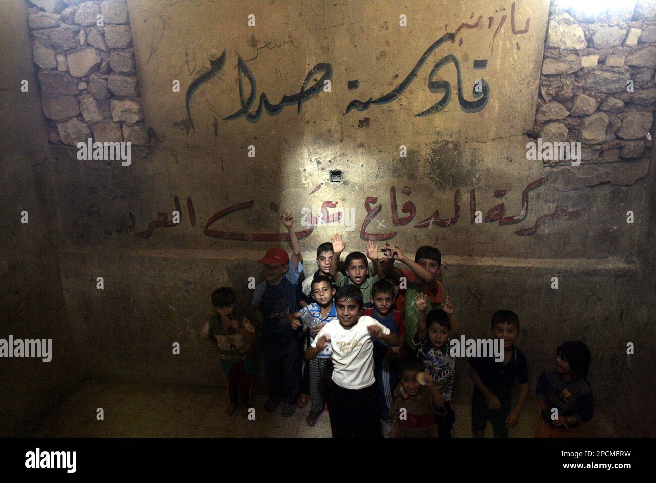 Iraqi Kurdish boys play in front of an Arabic writing on a wall reading ...