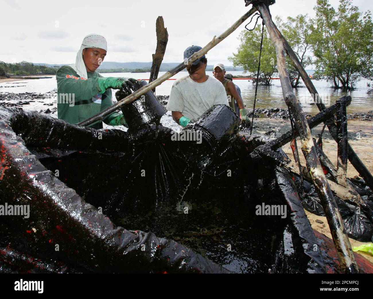Workers gather all collected bunker oil from the shoreline into a big ...