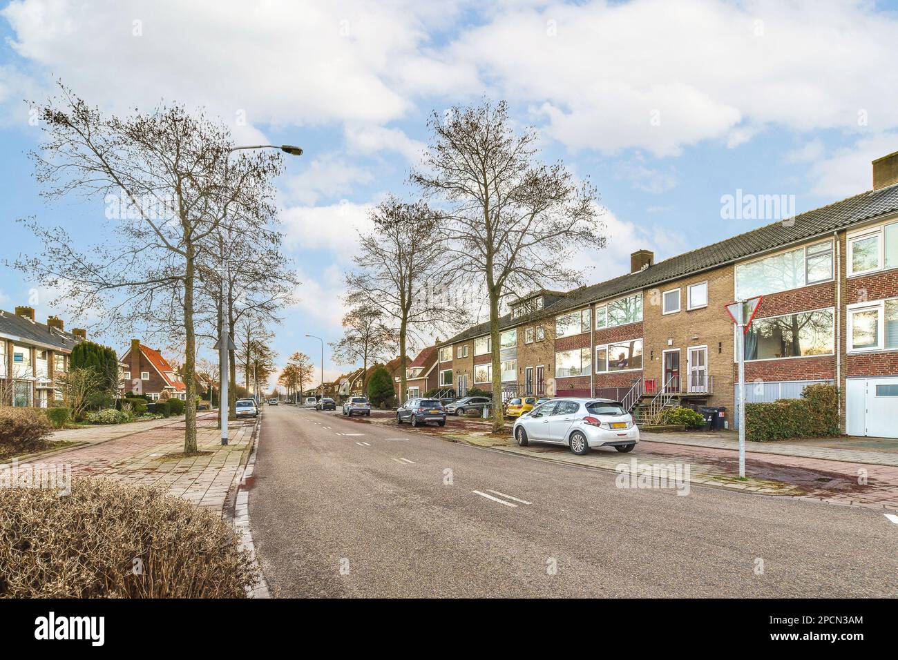 an empty street with cars parked on the side and houses in the back ...