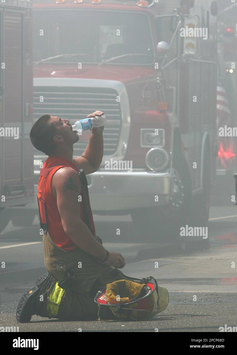 A firefighter takes a long drink from a bottle of water while fighting ...