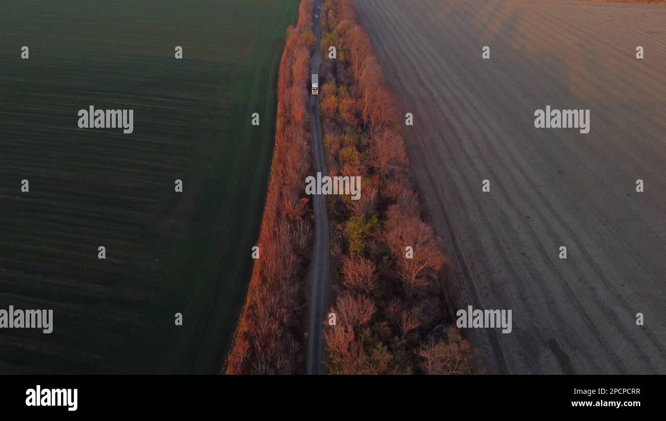 Large white cargo truck and car driving dirt road between agricultural ...