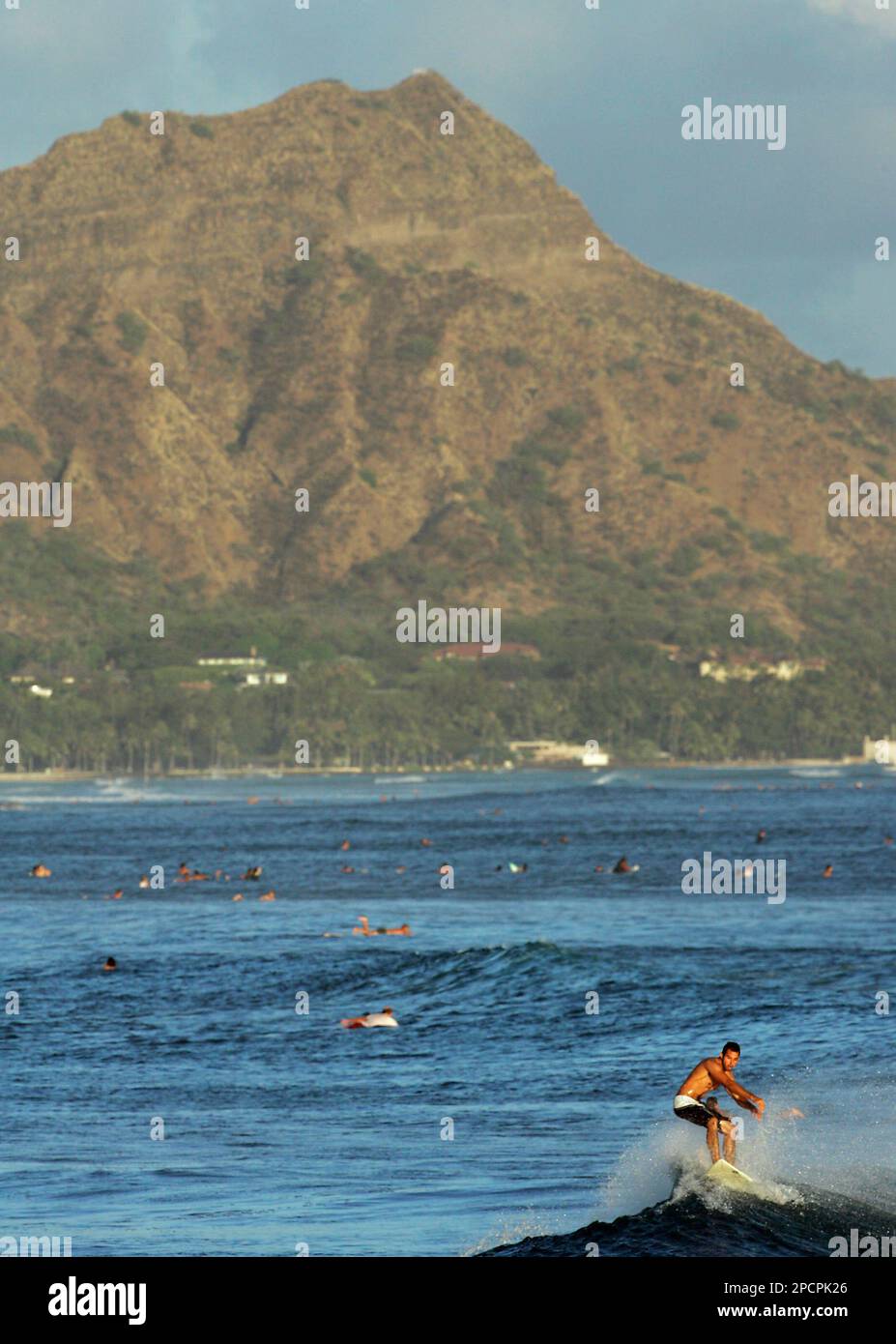 With Diamond Head crater in the background, a surfer rides a wave ...